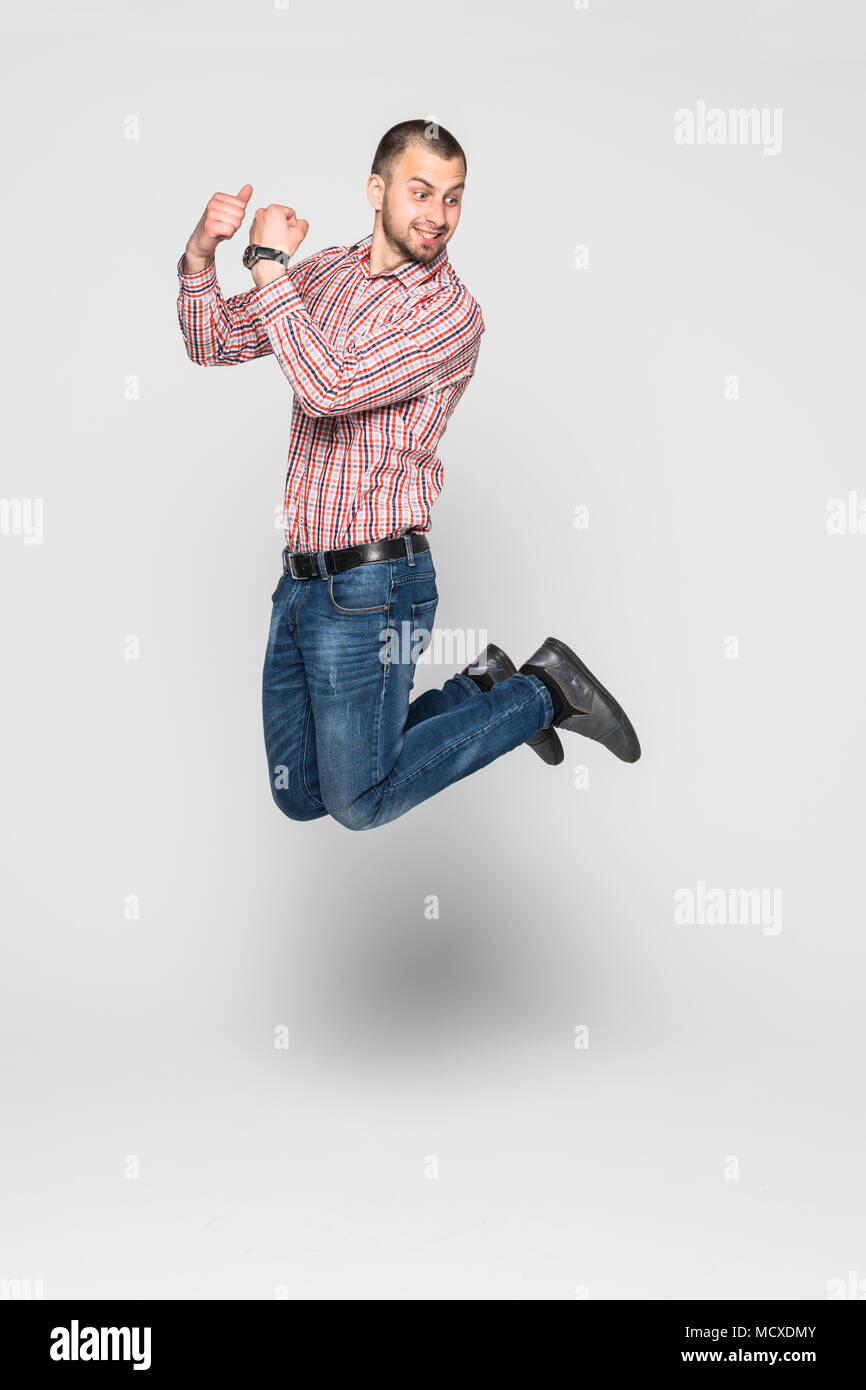 Vertical image of happy man in shirt and jeans which jumping in studio ...