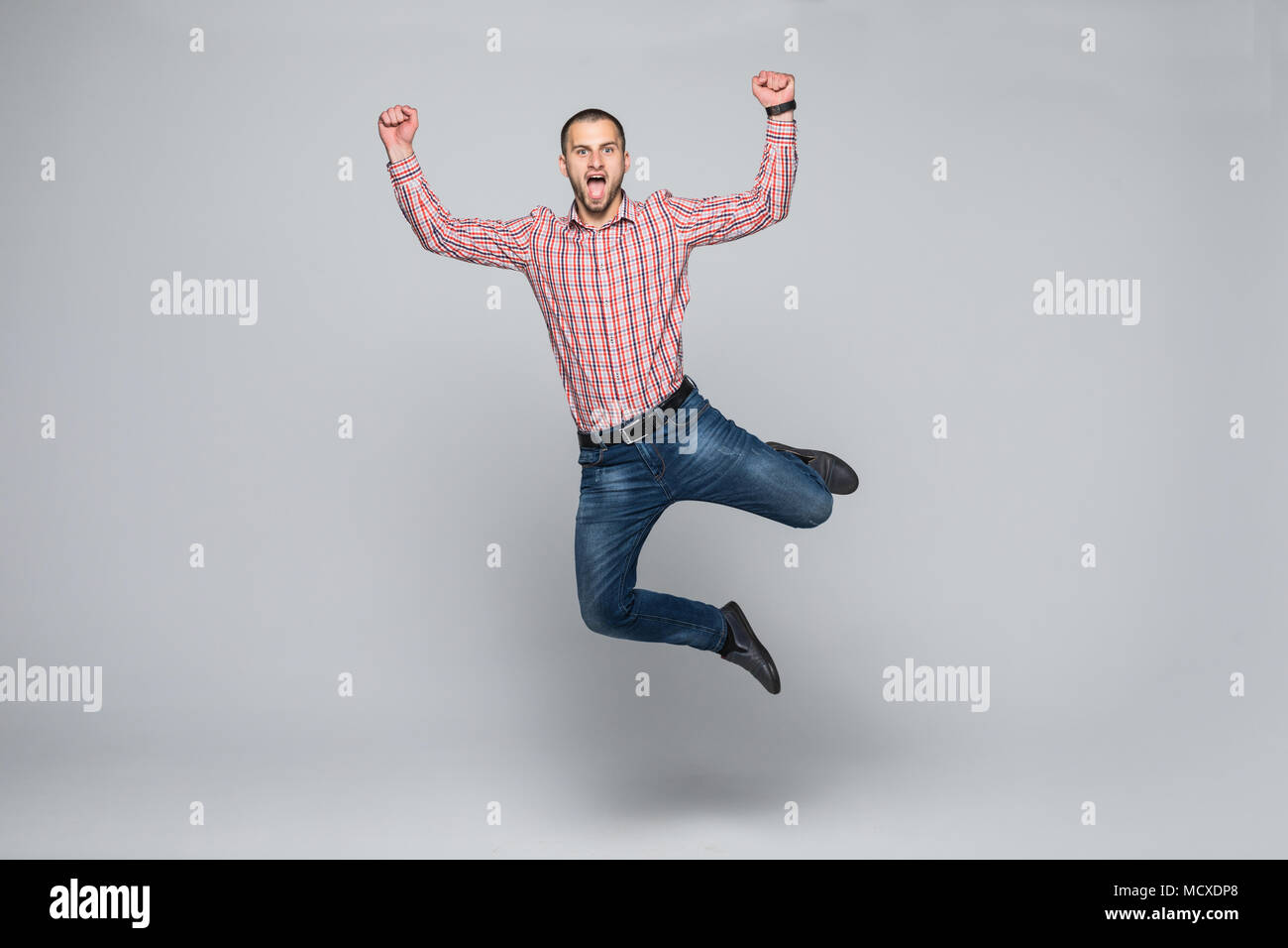 Vertical image of happy man in shirt and jeans which jumping in studio ...