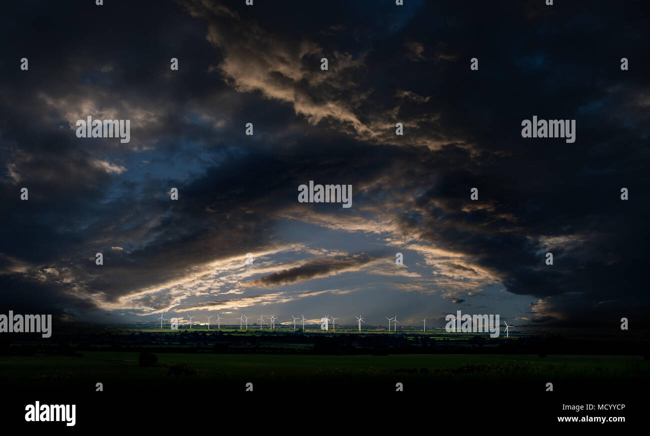 Wind farm with dramatic stormy clouds lighting the wind turbines ...
