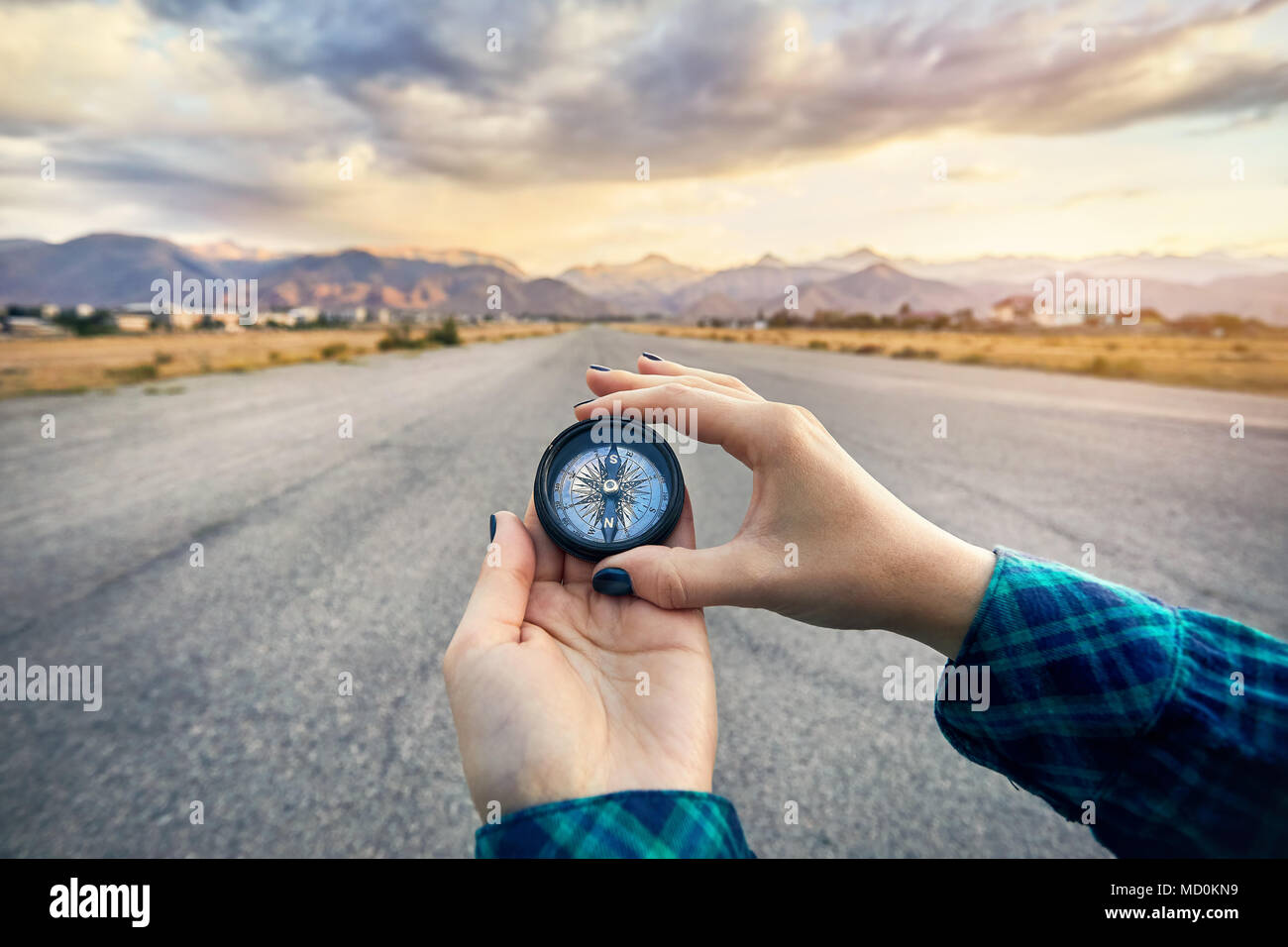 Woman hands in green shirt holding compass at sunrise sky background ...