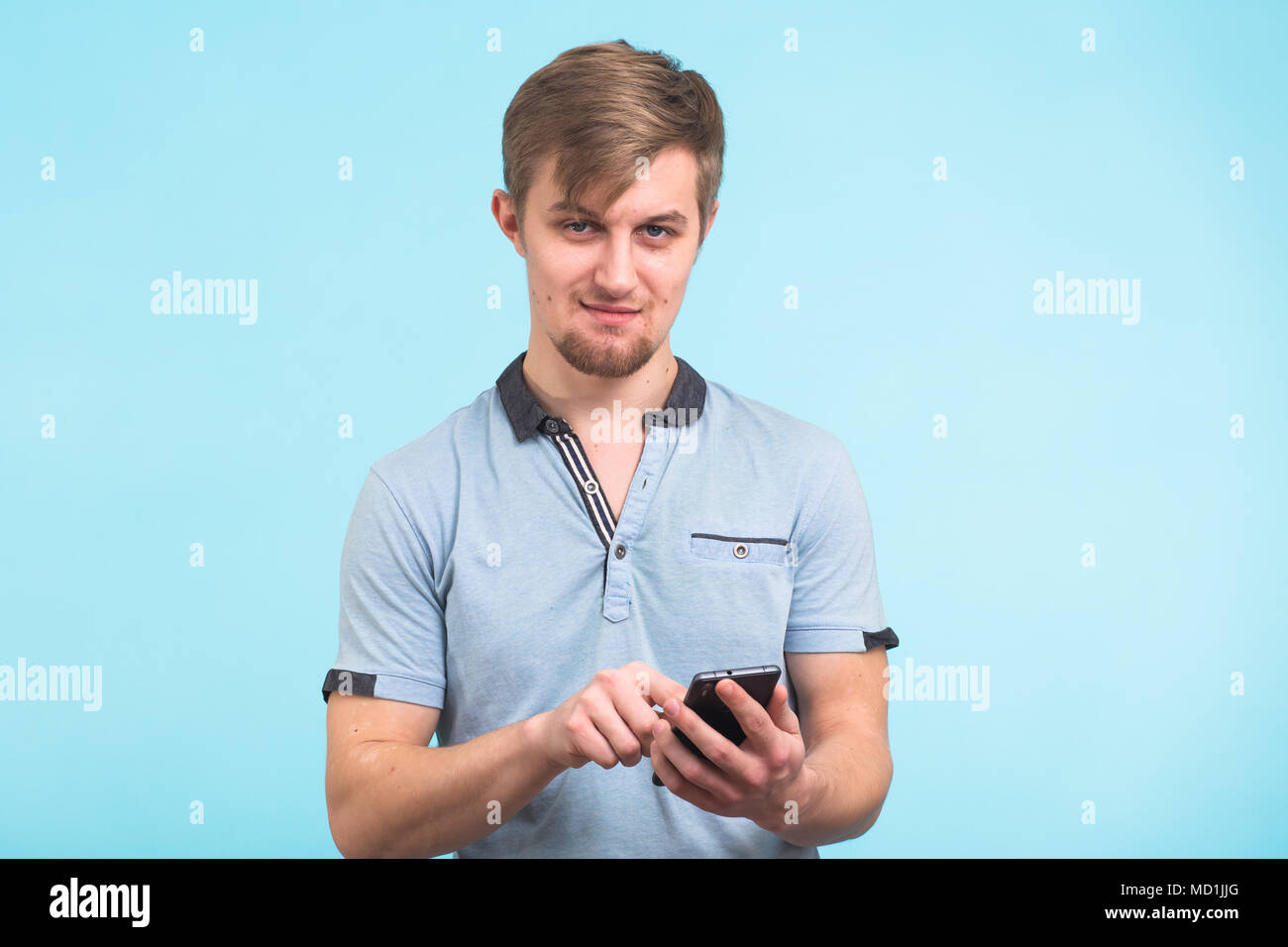 Young man typing text message on his cellphone against a blue ...