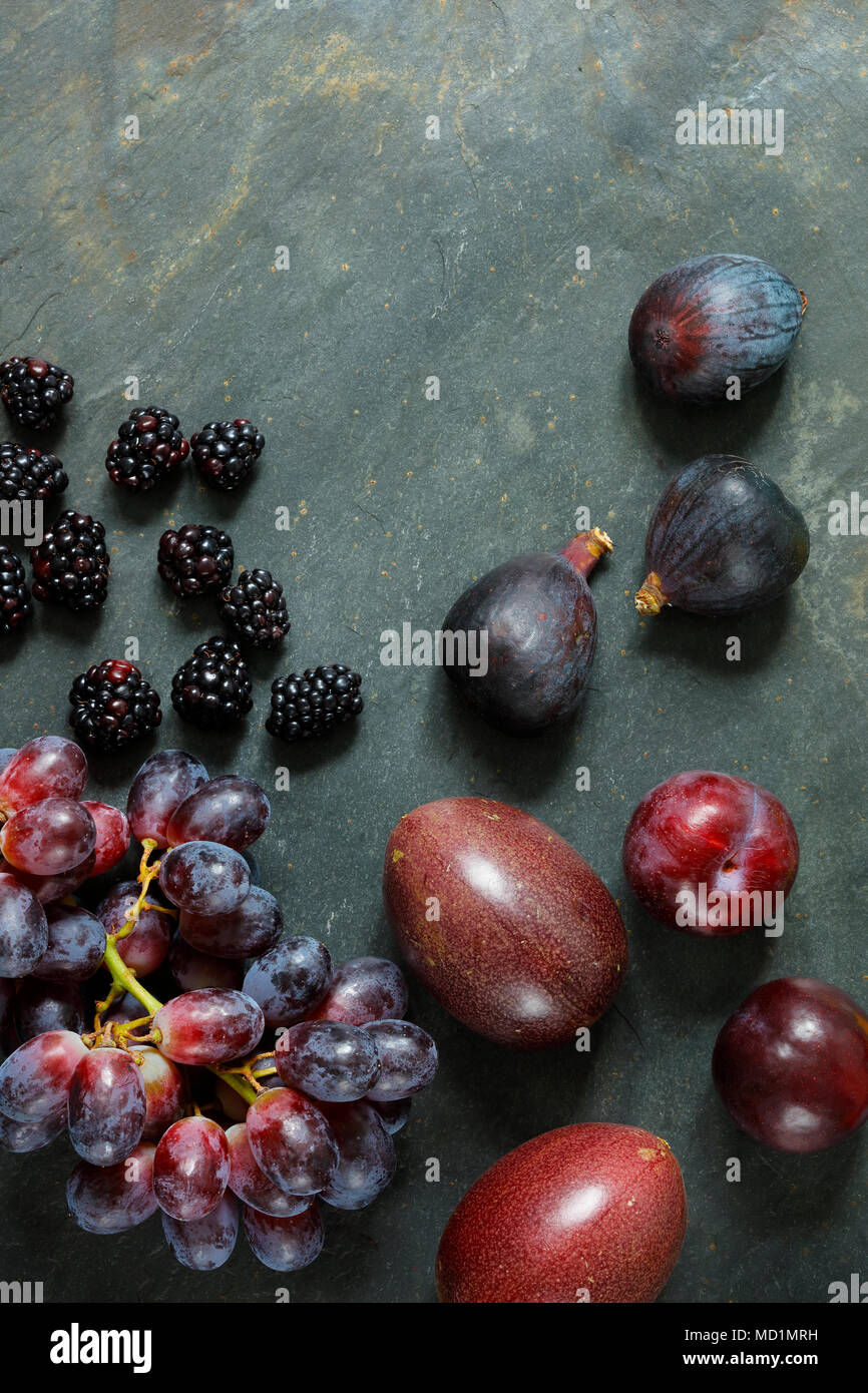 Dark Exotic Fruits on slate background including passion fruit, plums ...