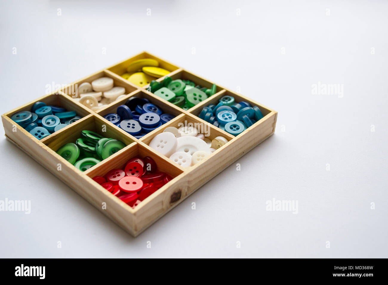 Clothes buttons in wooden box on white cardboard background. Closeup ...