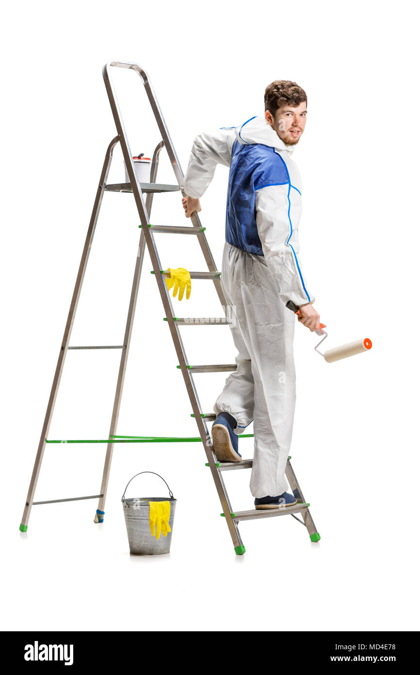 Young male decorator painting with a paint roller climbed a ladder ...