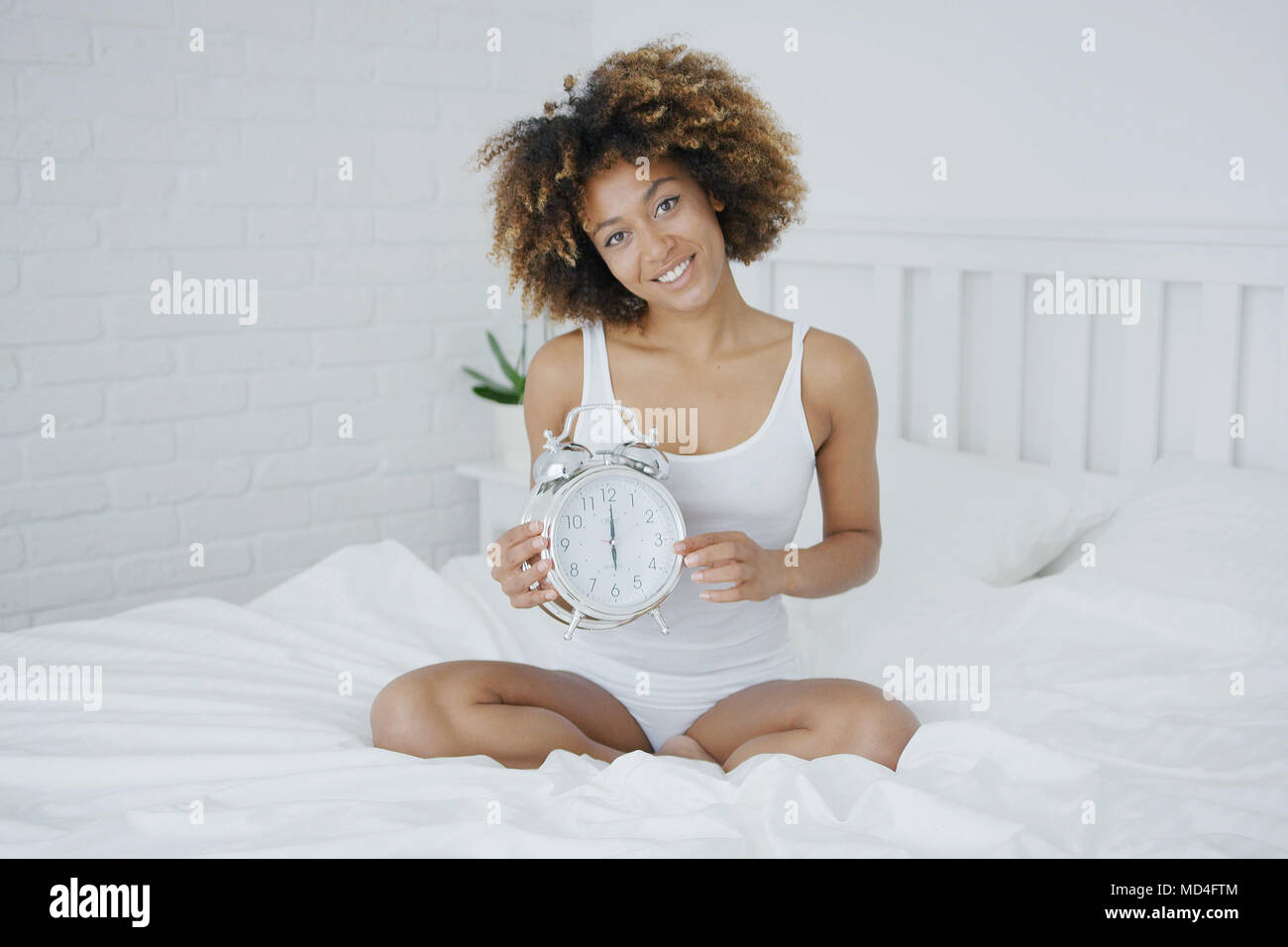 Charming woman posing on bed with clock Stock Photo - Alamy