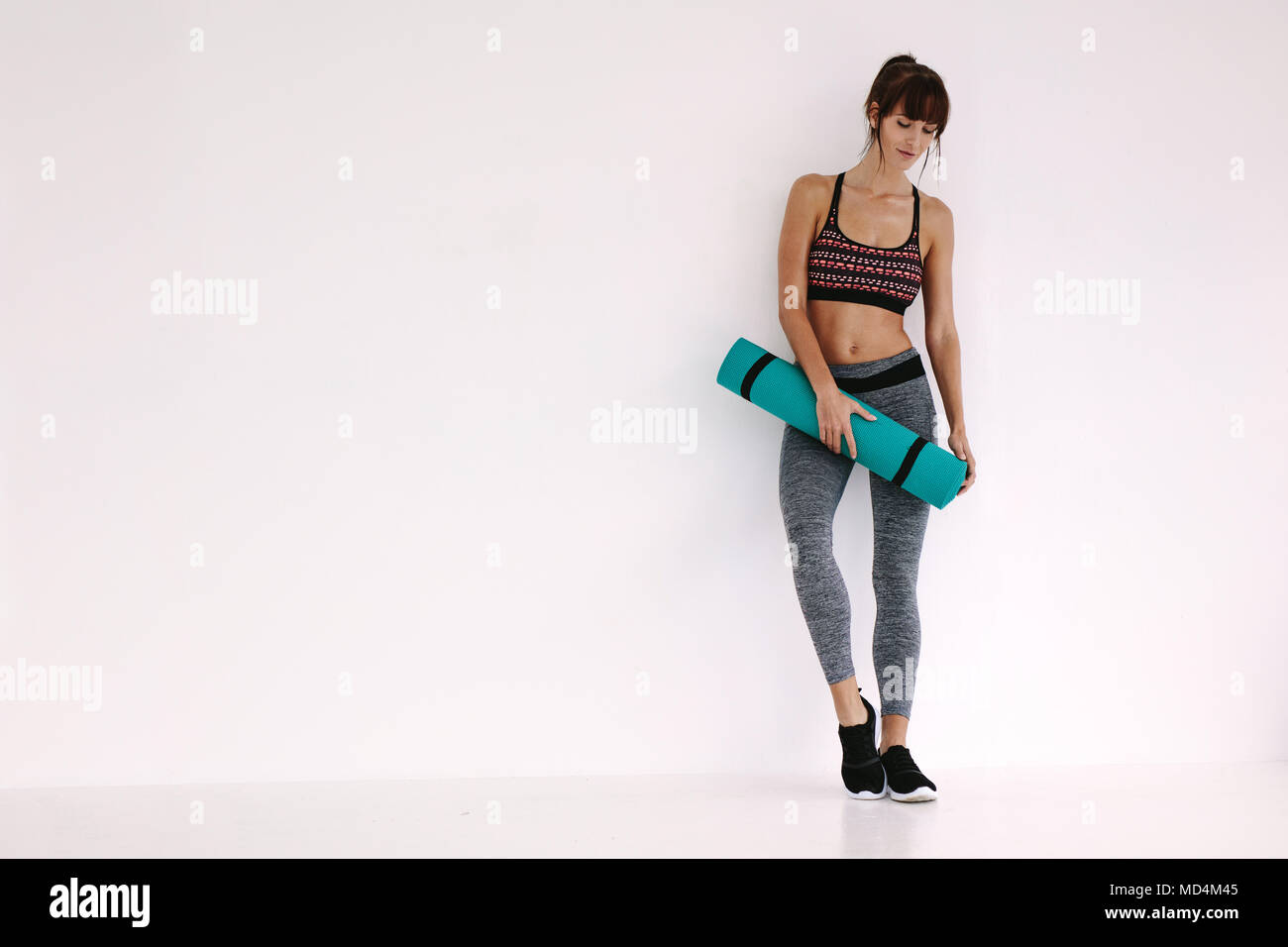 Young woman with slim healthy body standing with yoga mat in studio ...