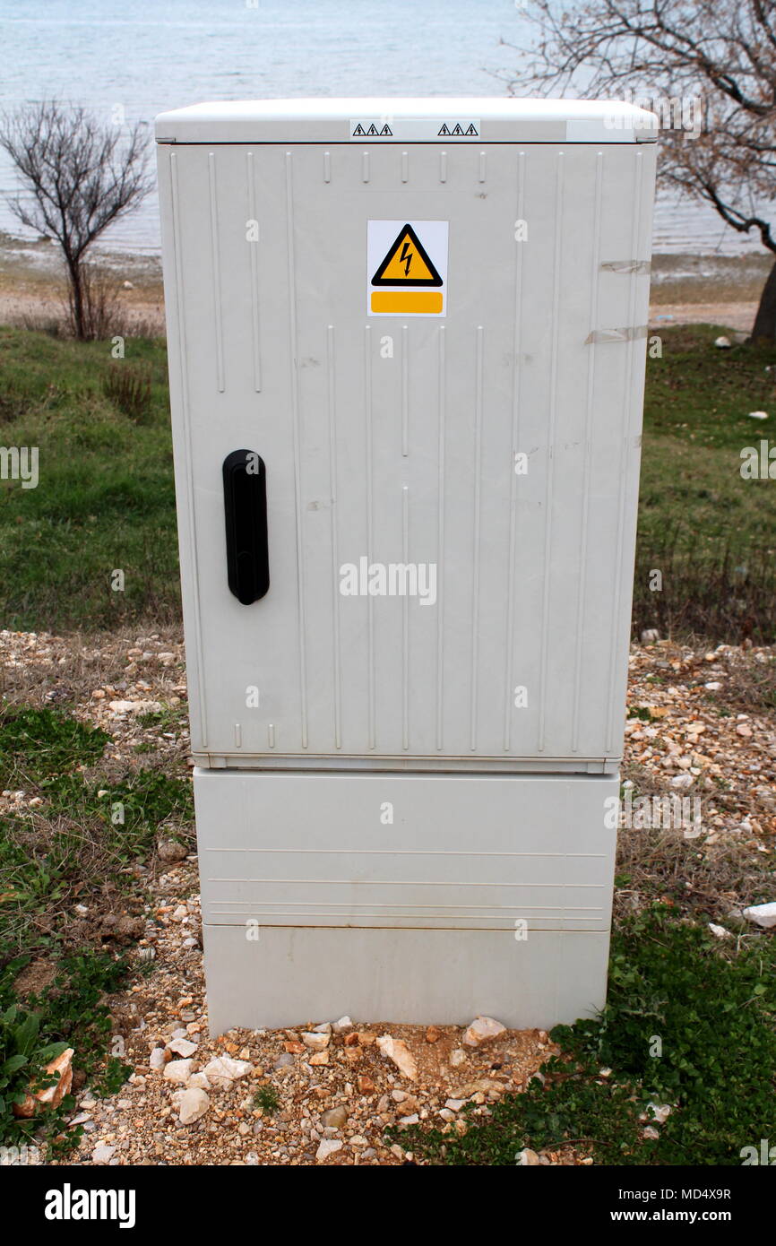 Outdoor grey electrical high voltage box surrounded with sand and uncut ...