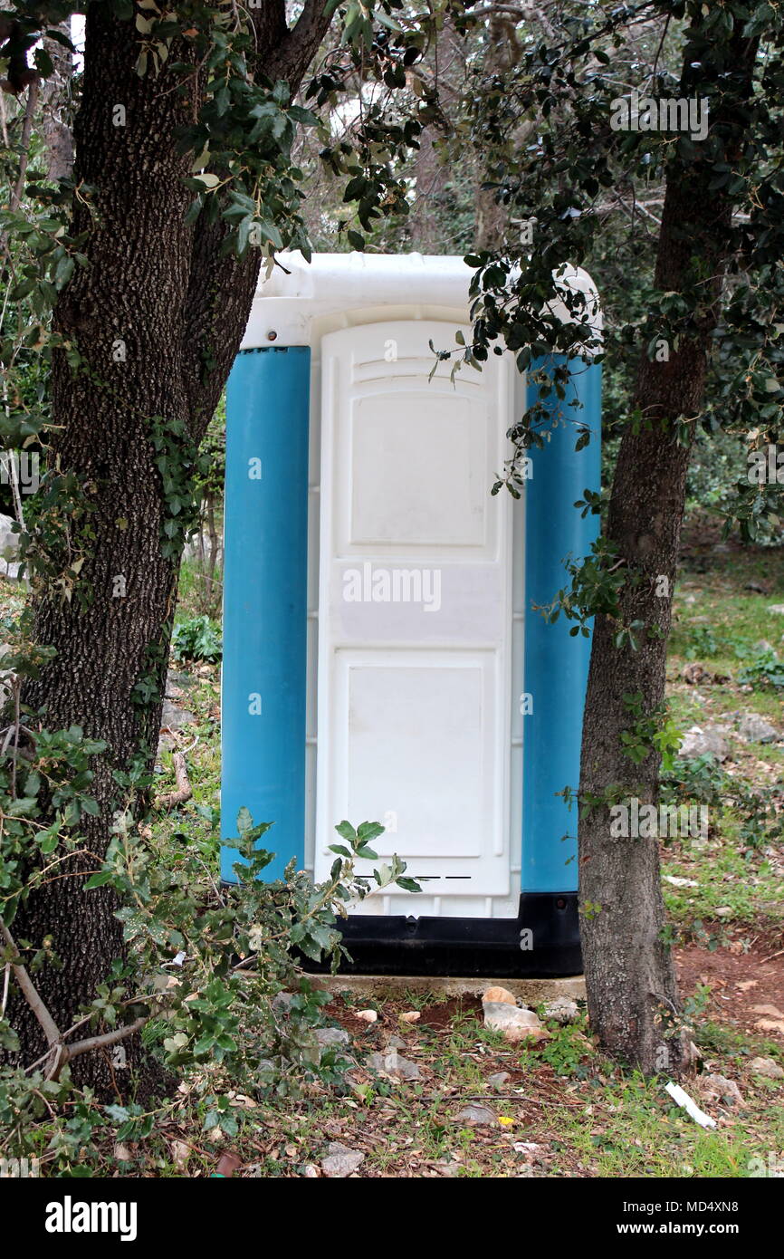Portable blue and white ecological toilet behind two tall trees in ...