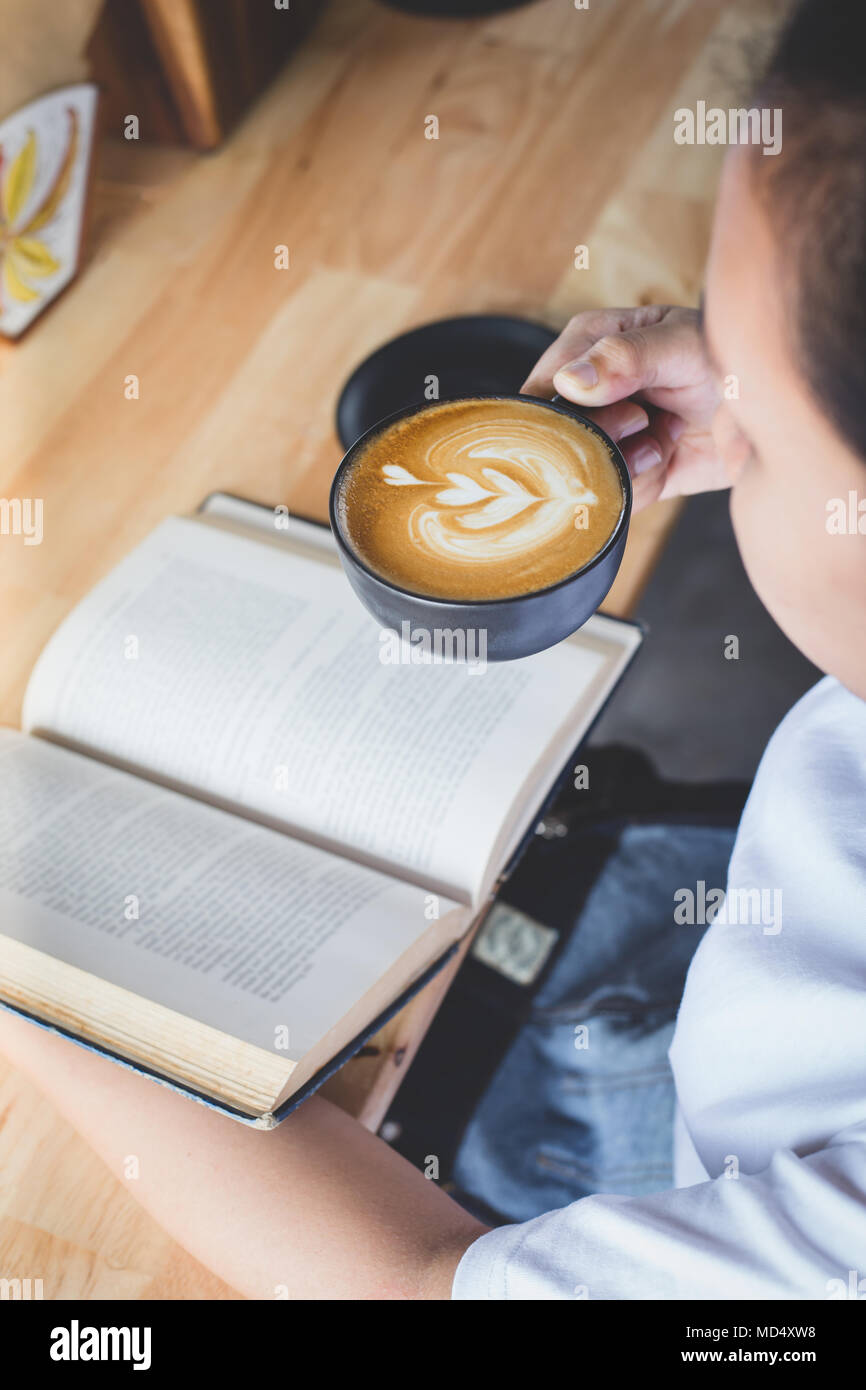 A girl reading book with drinking coffee latte with heart pattern in ...