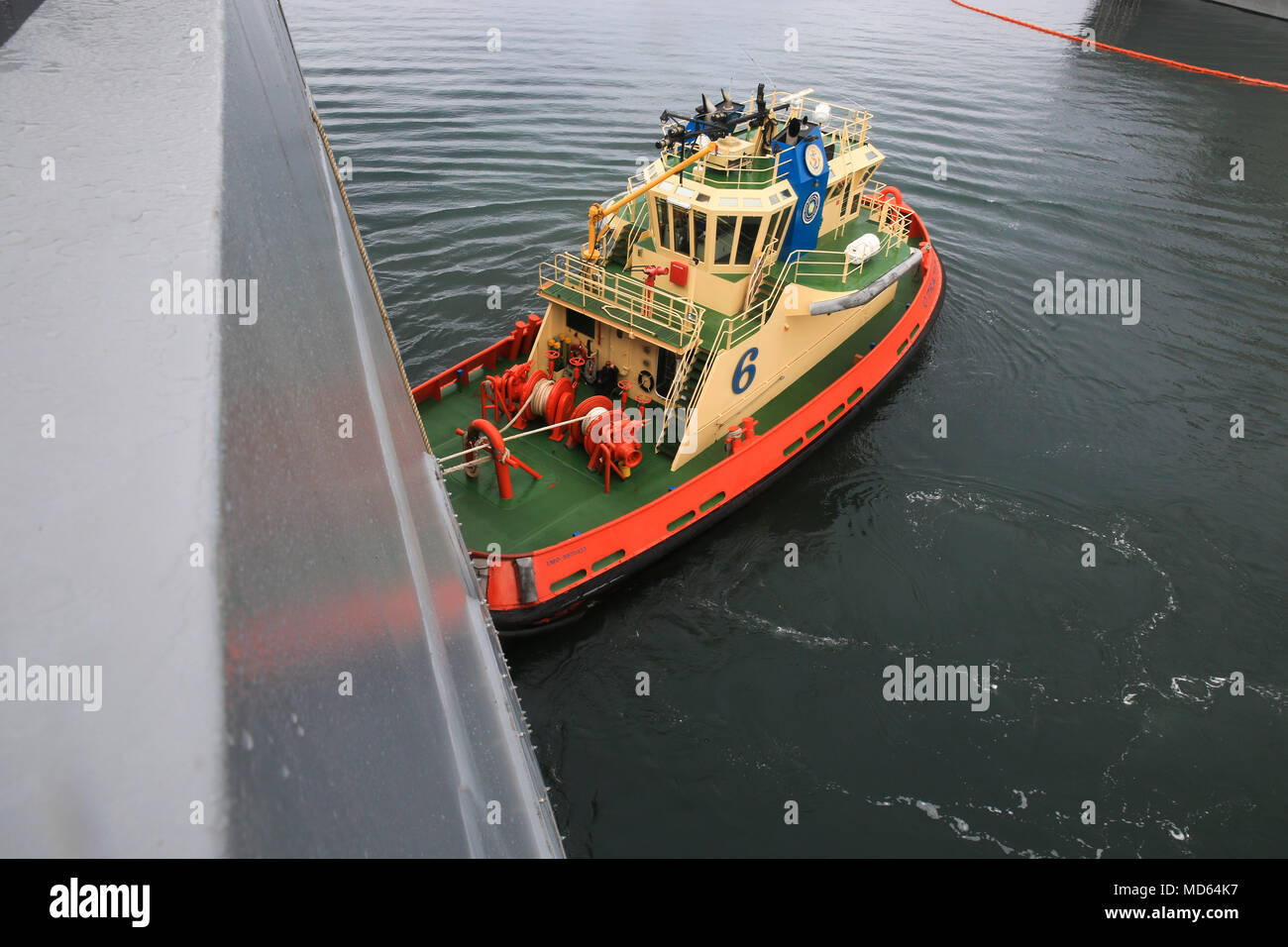 A tug boat helps guide the San Antonio-class amphibious transport dock ...