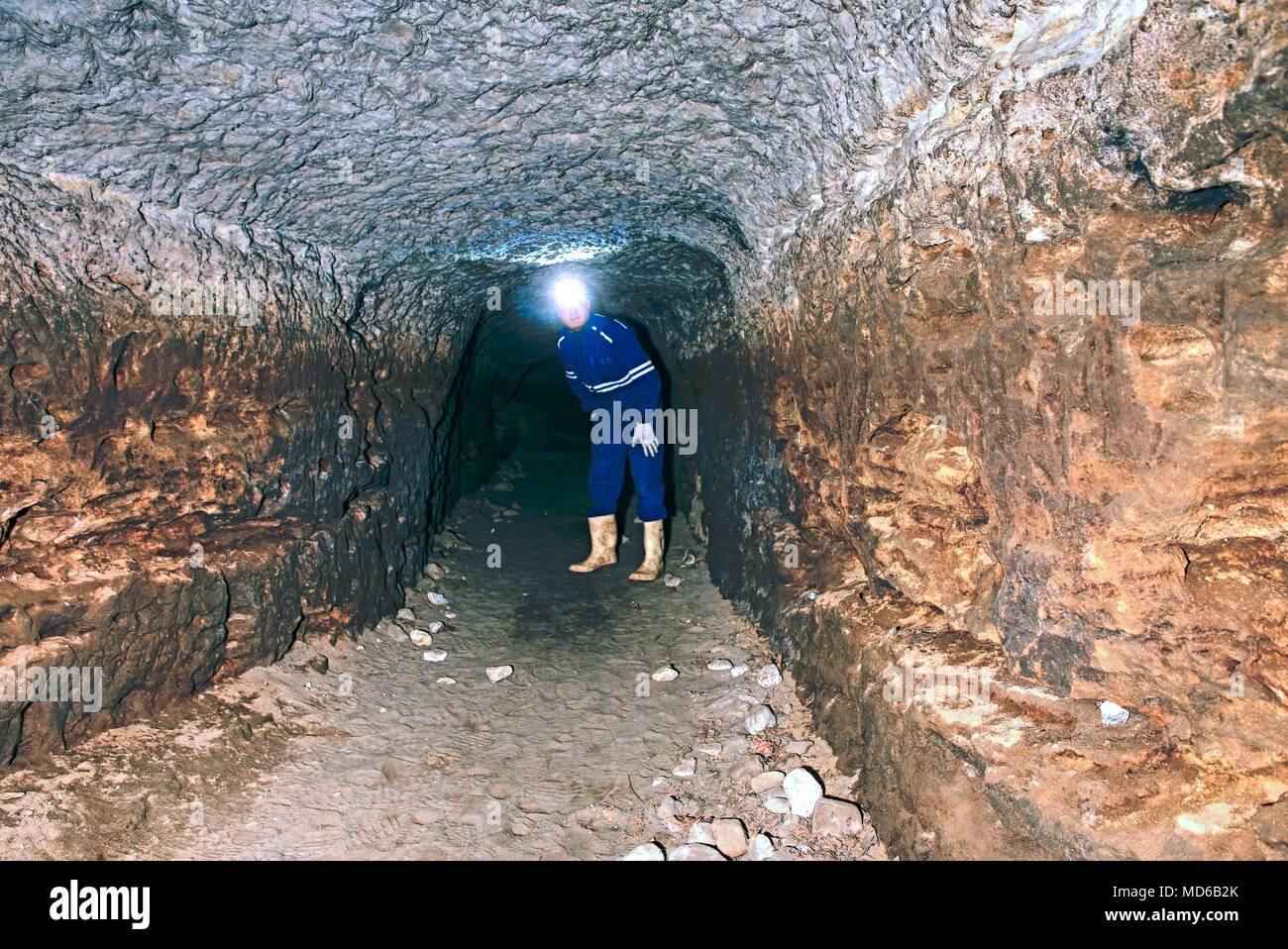 Underground work. Hunched worker in a blue overall and a safety helmet ...