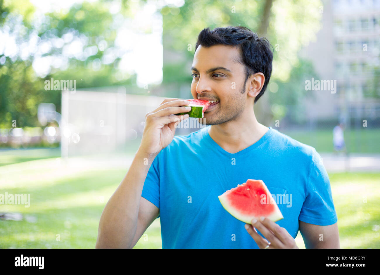 Closeup portrait, guy in blue shirt chowing down on watermelon wedge ...