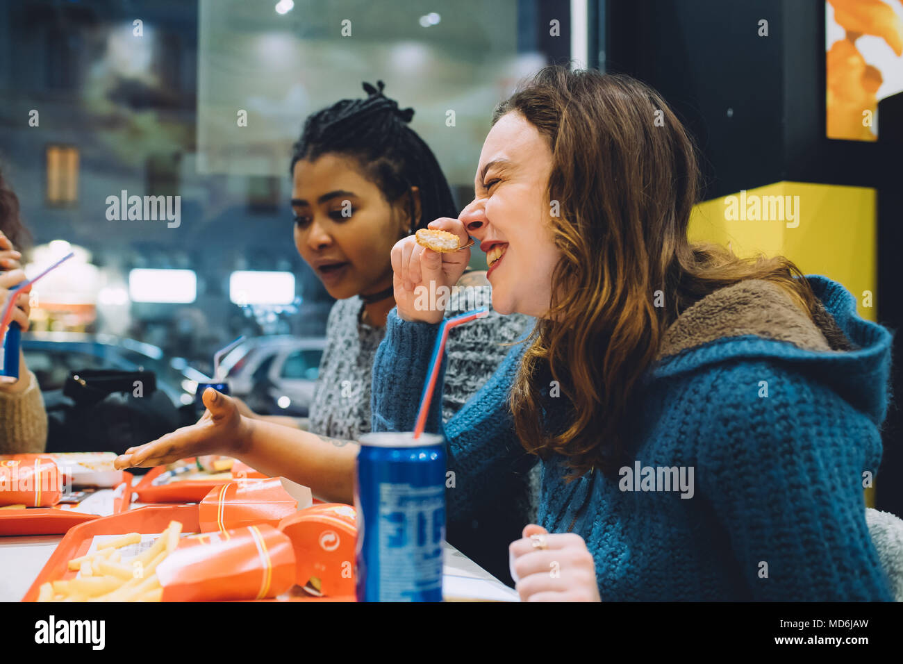 two young women multiethnic indoor eating at fast food - food and drink ...