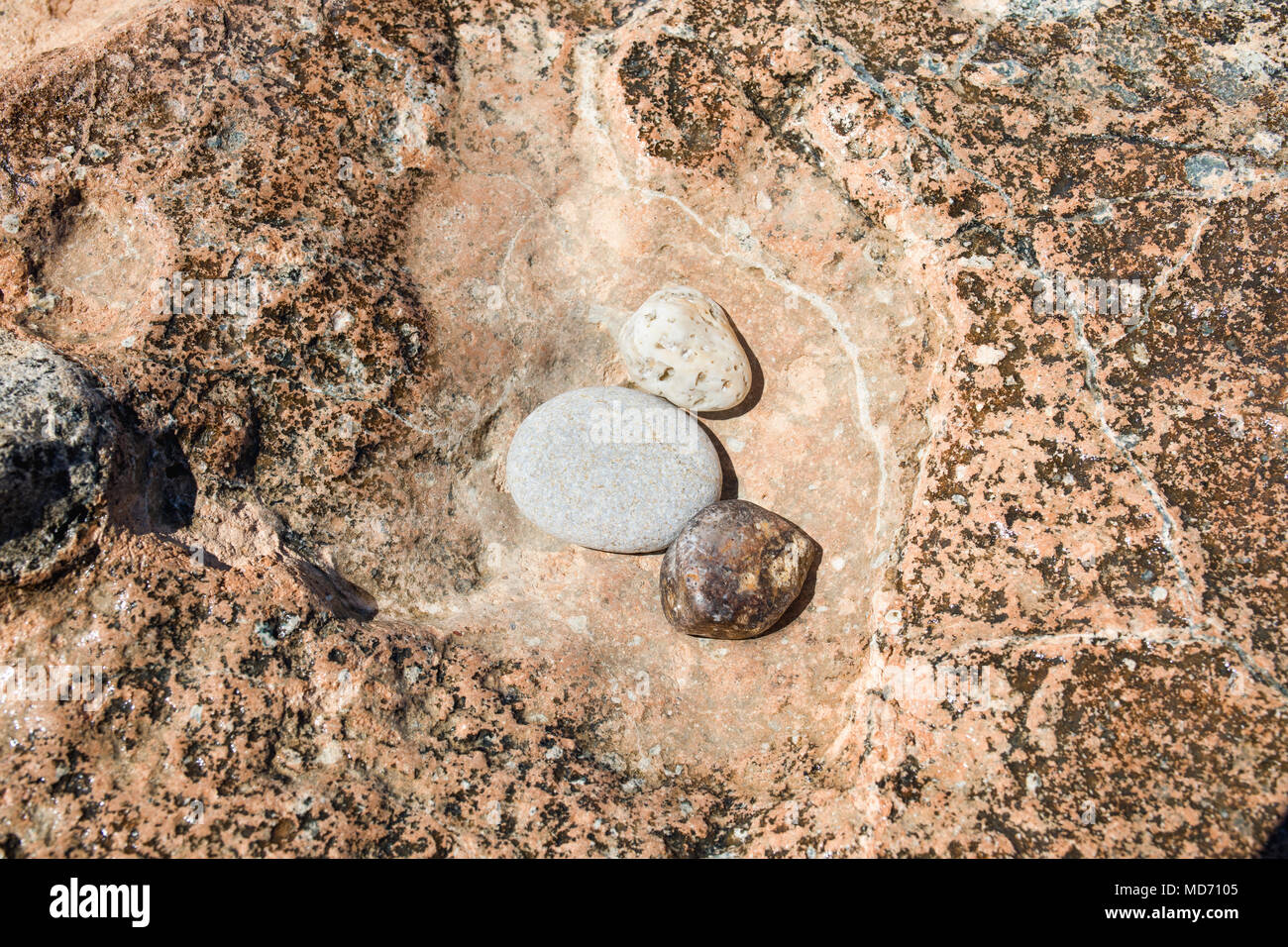 Round shaped stones in a hollow on a rocky ledge. Crete coast, shore ...