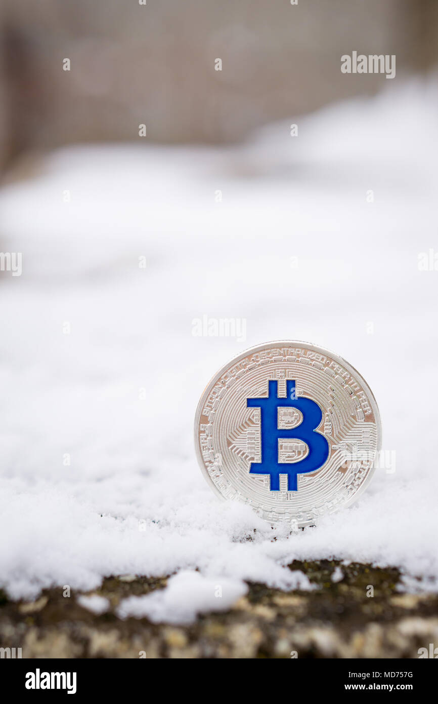 A silver colored Bitcoin placed in snow on concrete. Isolated scene of ...