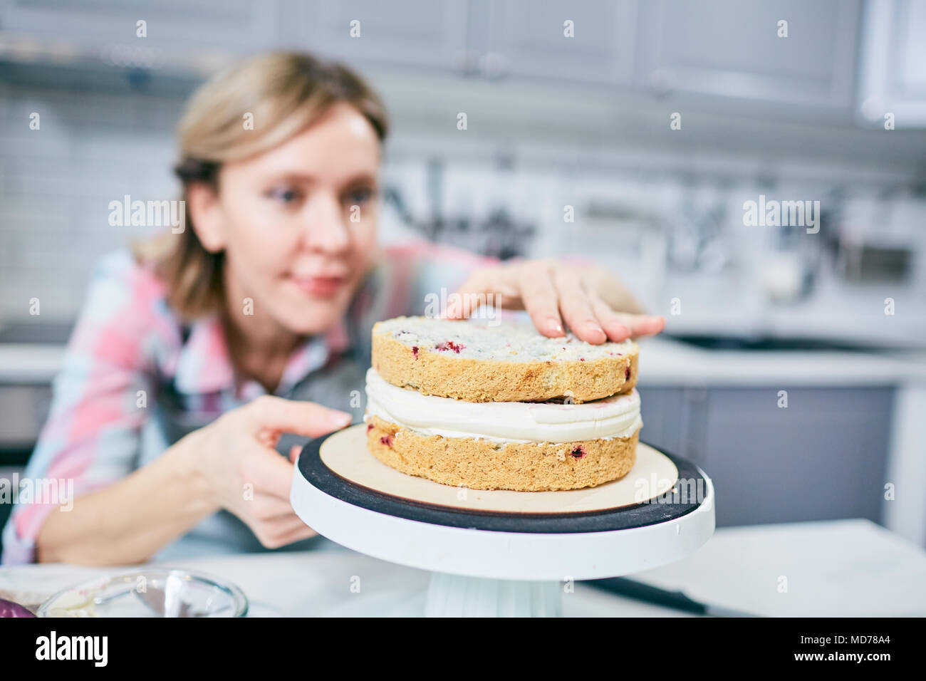Defocused Caucasian female cook finishing appetizing layer cake with ...