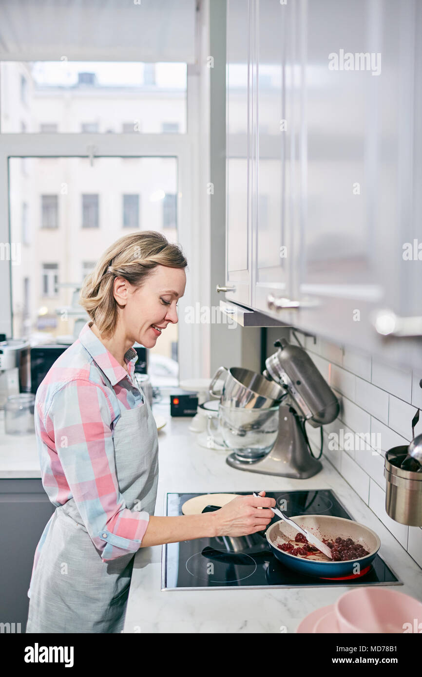 Side view of good-looking Caucasian woman preparing meal in frying pan ...