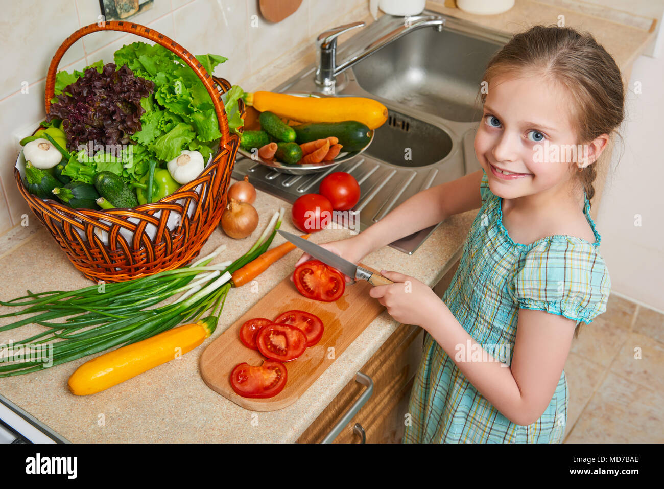 Child girl cooking in home kitchen, chopping tomatoes. Basket of ...