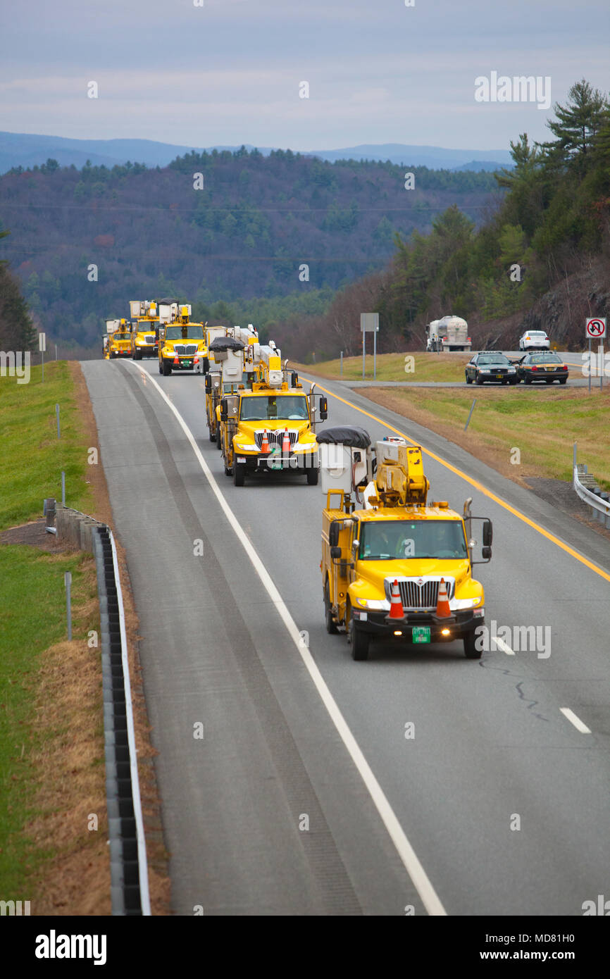 A convoy of yellow electric utility trucks in formation heading south ...