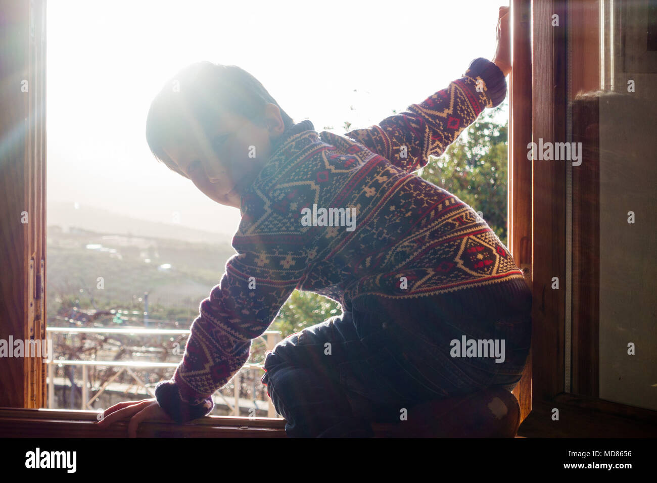 Boy looking at camera while sitting on the window, Greece Stock Photo ...