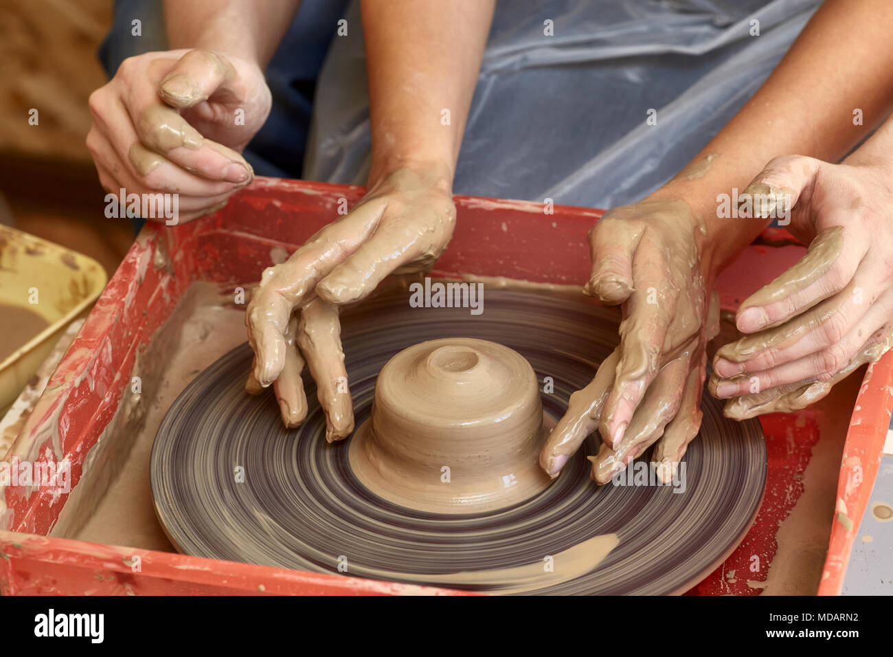 Hands of two people create pot on potter's wheel. Teaching pottery ...