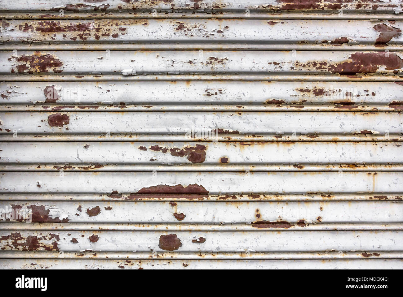 Old damaged white rolling steel door. A shutter totally rusted, closed ...