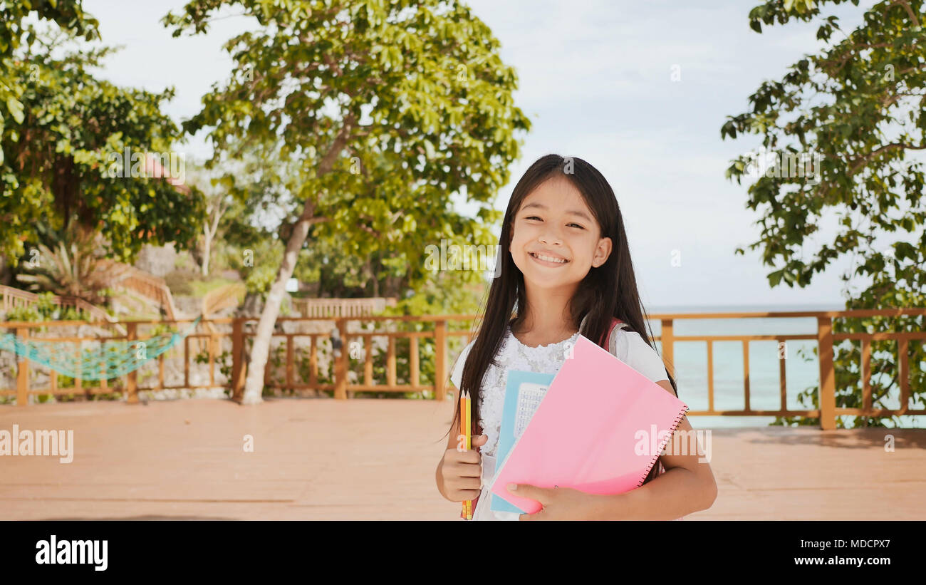 A charming filipino schoolgirl with a backpack and books in a park off ...