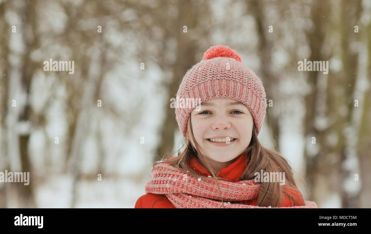 A young schoolgirl joyfully throws a snowball and breaks it with a palm ...