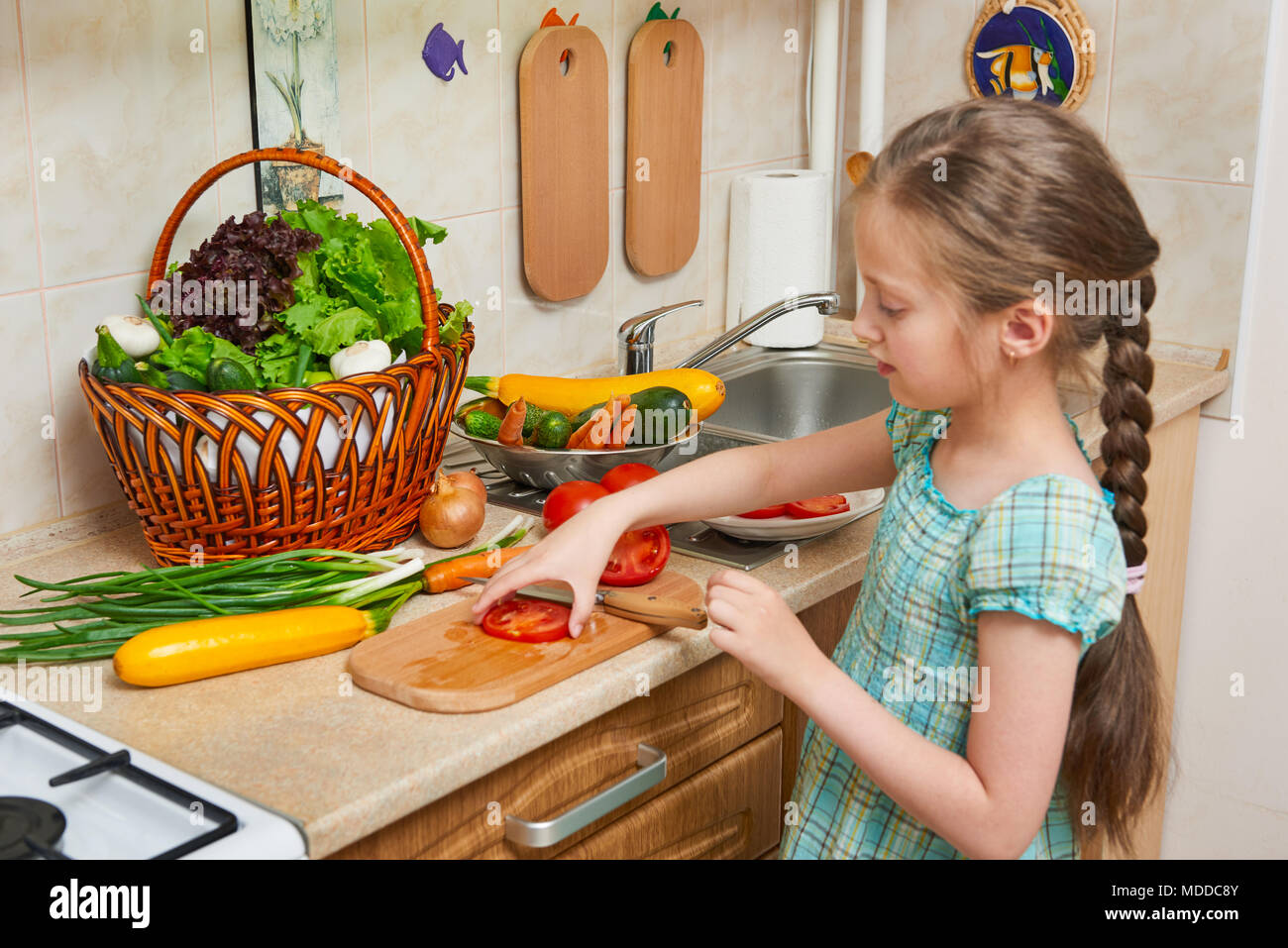 Child girl cooking in home kitchen, chopping tomatoes. Basket of ...