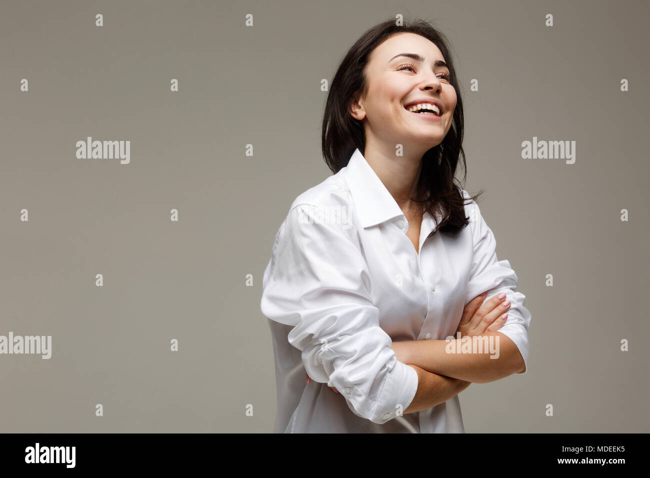 Beautiful girl in a white shirt shows emotions - smile, fun. On a light ...