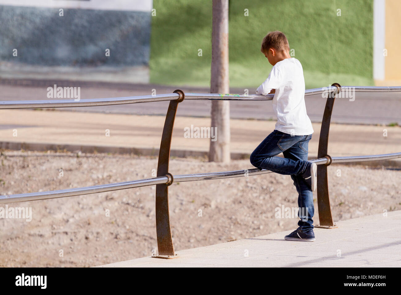 Kid boy standing alone on the bridge and looking down to the water ...