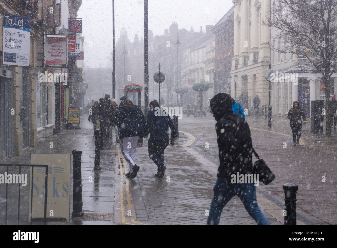 People walk through a snowy outdoor market with stalls selling produce ...