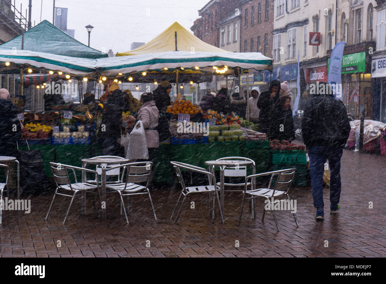 People walk through a snowy outdoor market with stalls selling produce ...