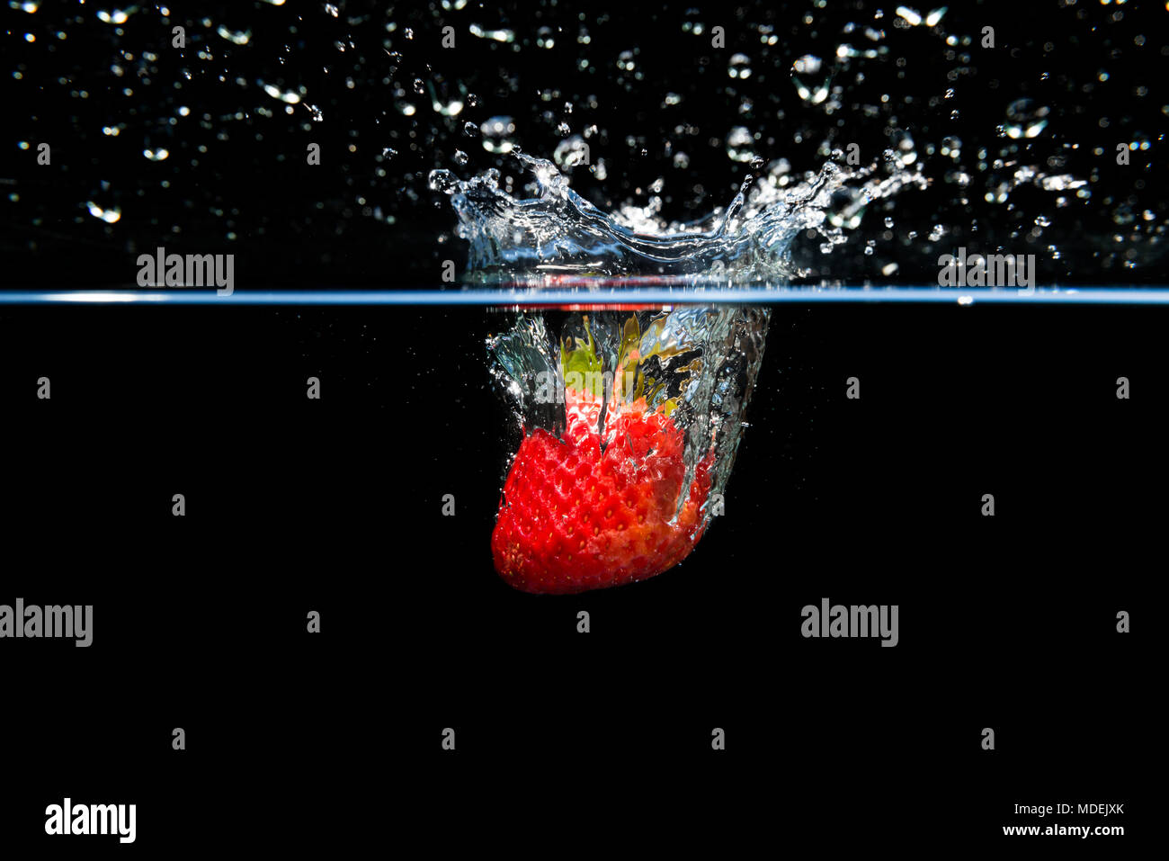 Strawberry falling into the water and splashing drops on black ...