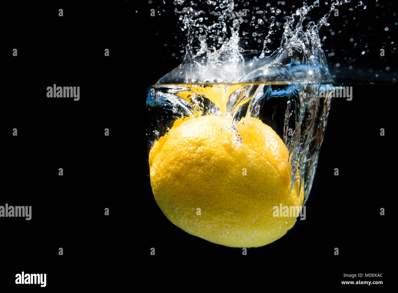 Lemon falling into the water and splashing drops on black background ...