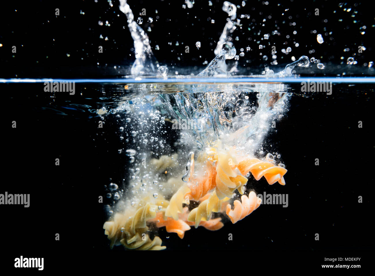 Pasta spirals falling into the water and splashing drops on black ...