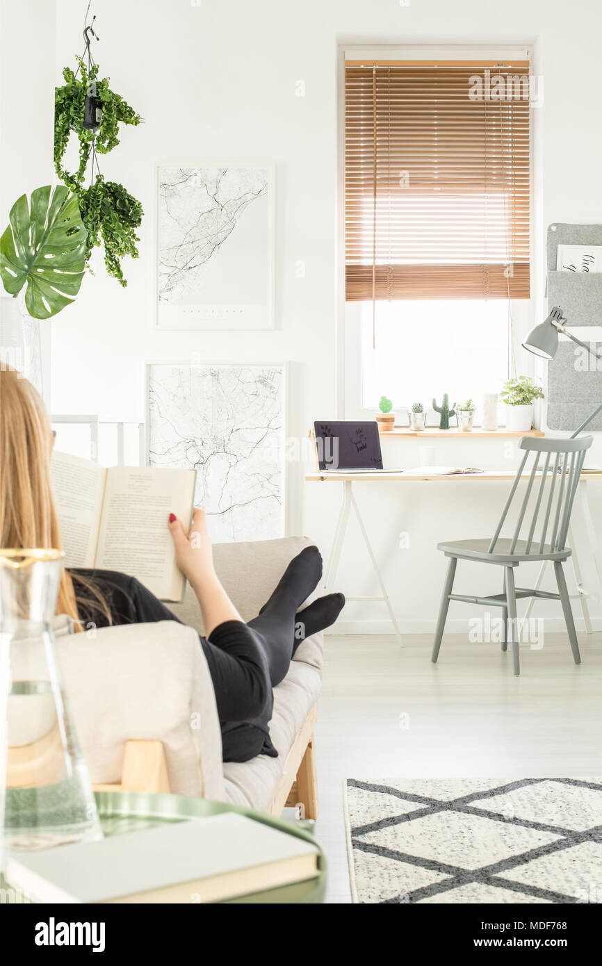 Girl reading a book while lying on a couch in a bright home office ...