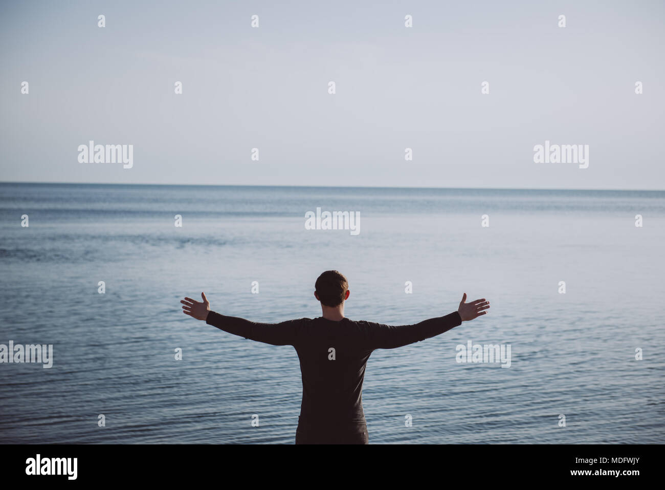 Man standing by the ocean with his arms outstretched Stock Photo - Alamy