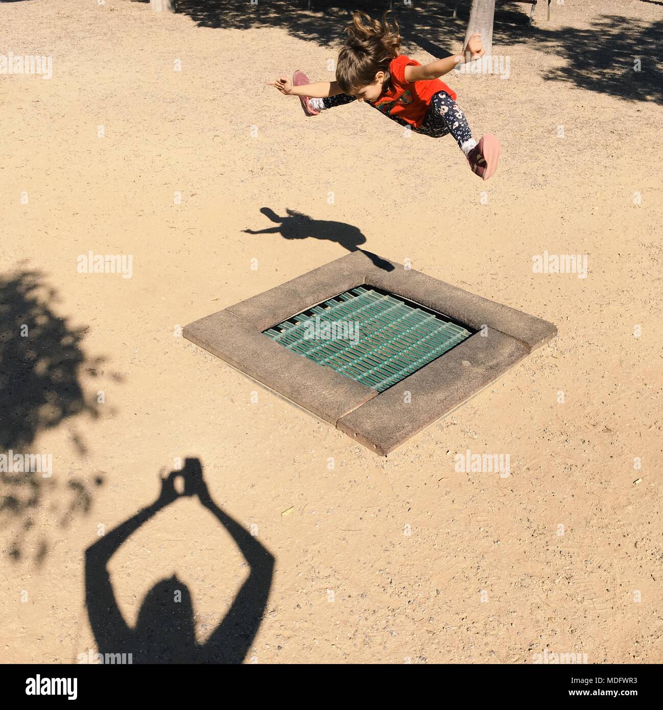 Mother photographing her daughter jumping over a metal grate Stock ...