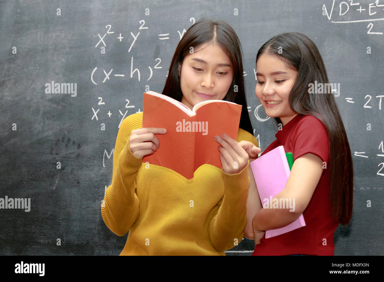 Two happy Asian college student reading books in the library together ...