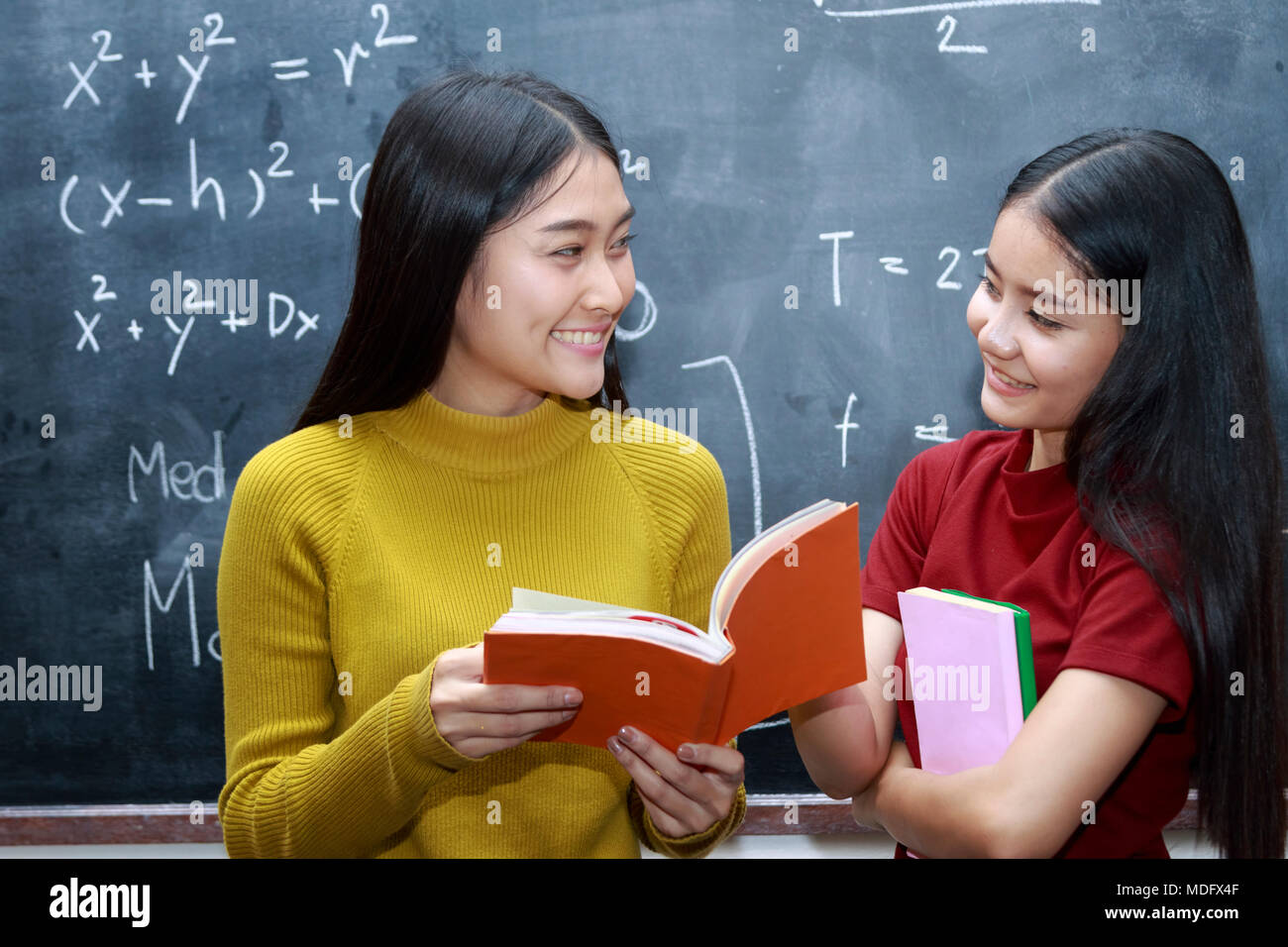 Two happy Asian college student over blackboard reading books together ...