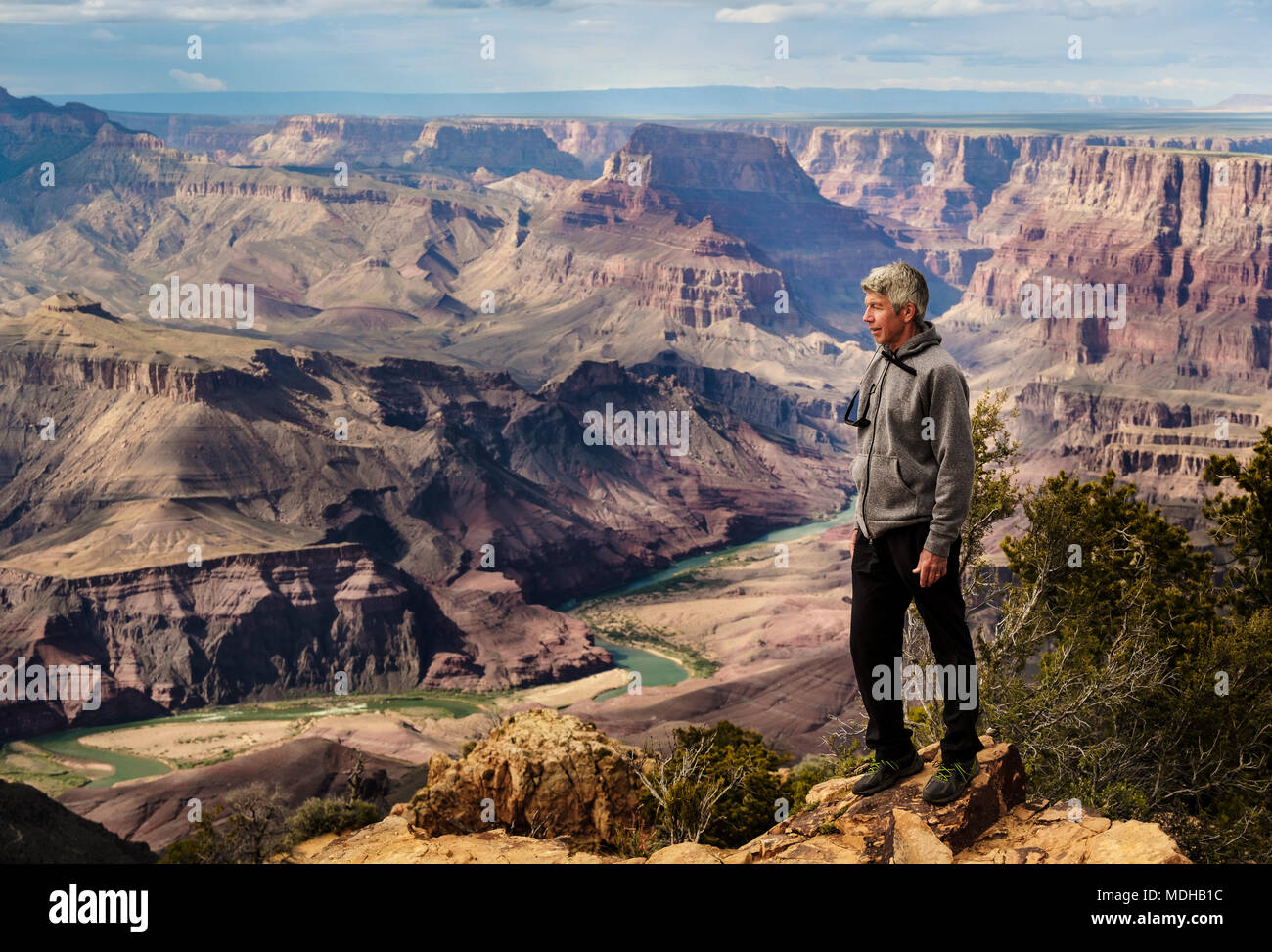 A senior man hiking in the Grand Canyon and standing on a ridge looking ...