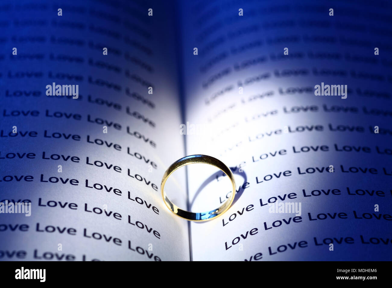 Single gold wedding ring on an open book with the word love repeated ...