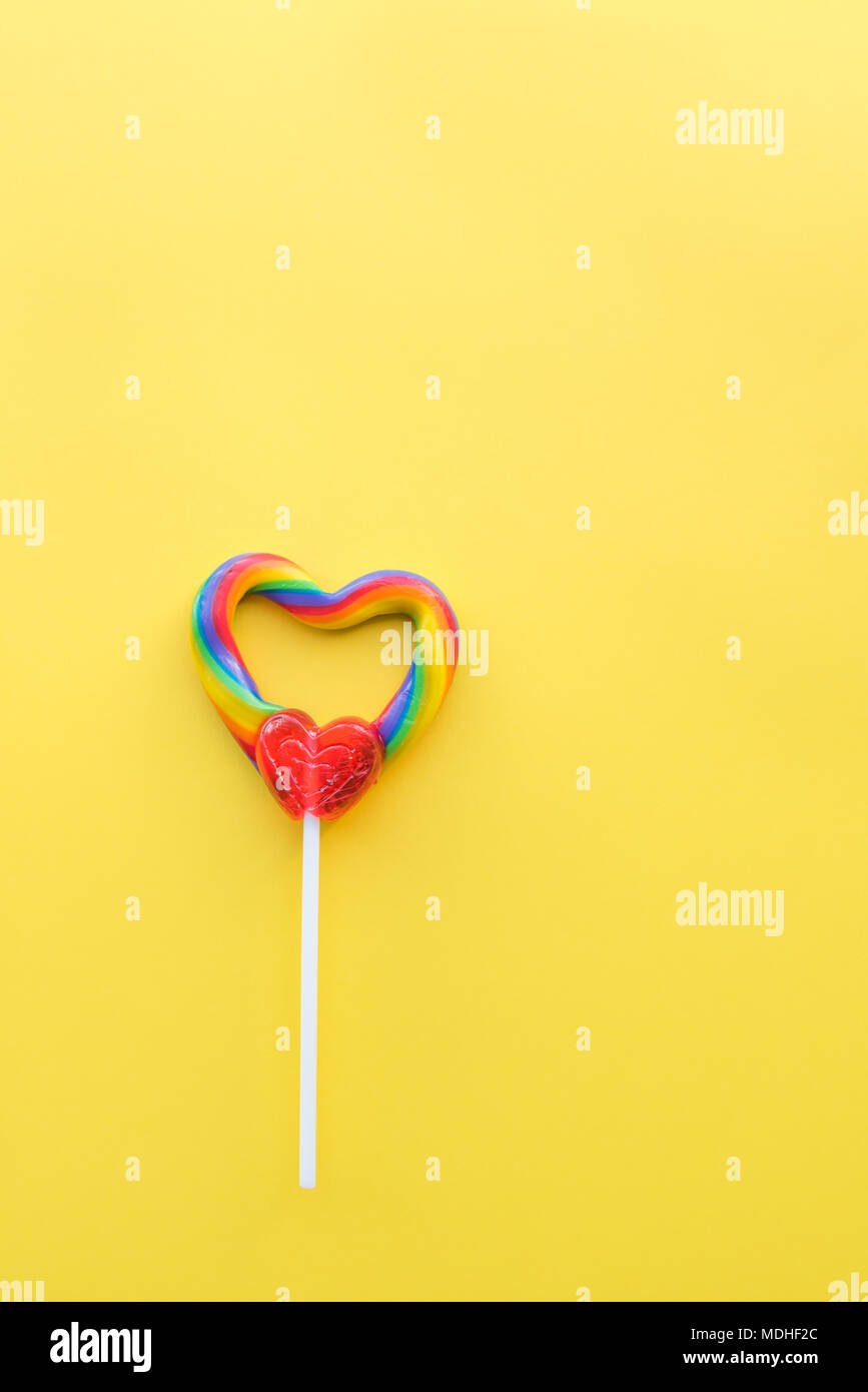 Cute heart-shaped rainbow swirl lollipop on solid yellow background ...