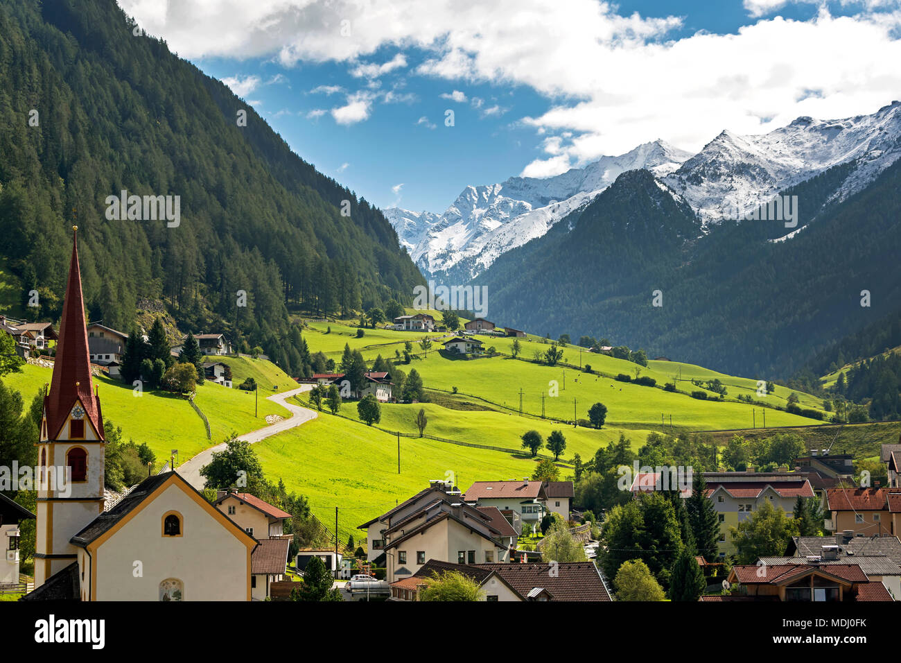 Alpine village with church steeple, green meadows in the valley and ...