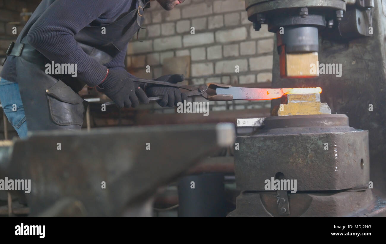 Man blacksmith forges the metal at the mechanical hammer Stock Photo ...