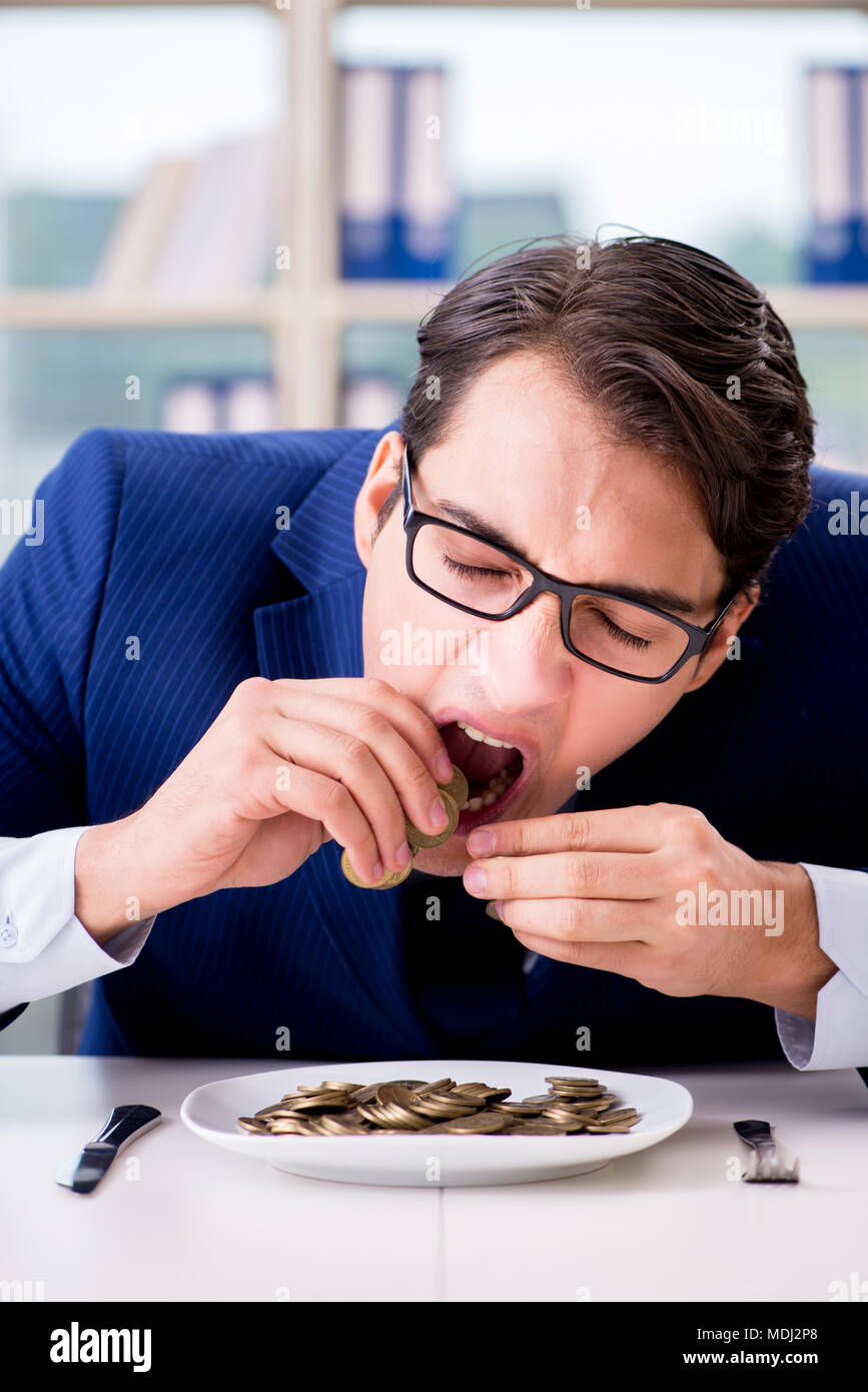 Funny businessman eating gold coins in office Stock Photo - Alamy