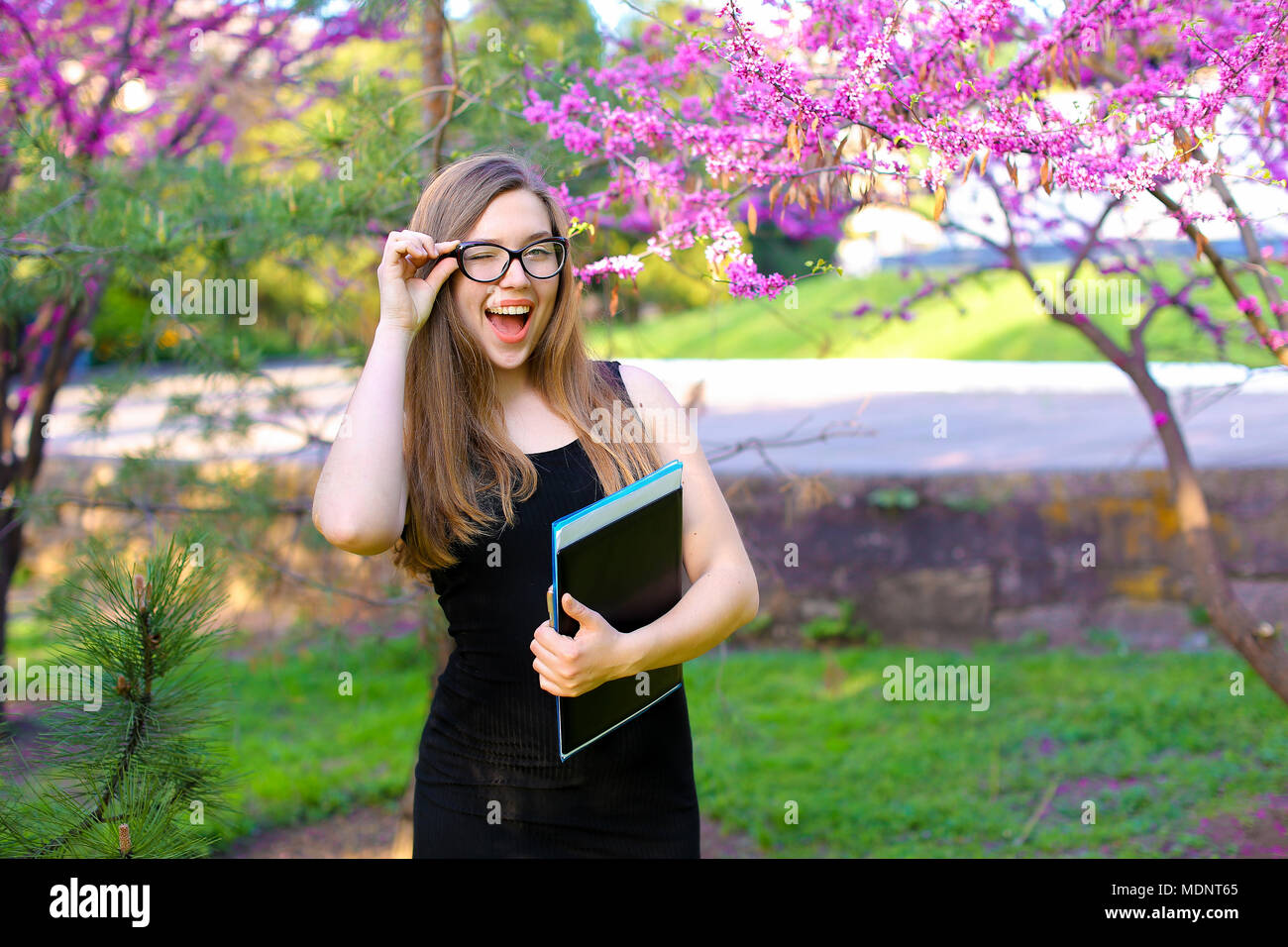 Female intelligent student touching glasses in garden and standing with ...