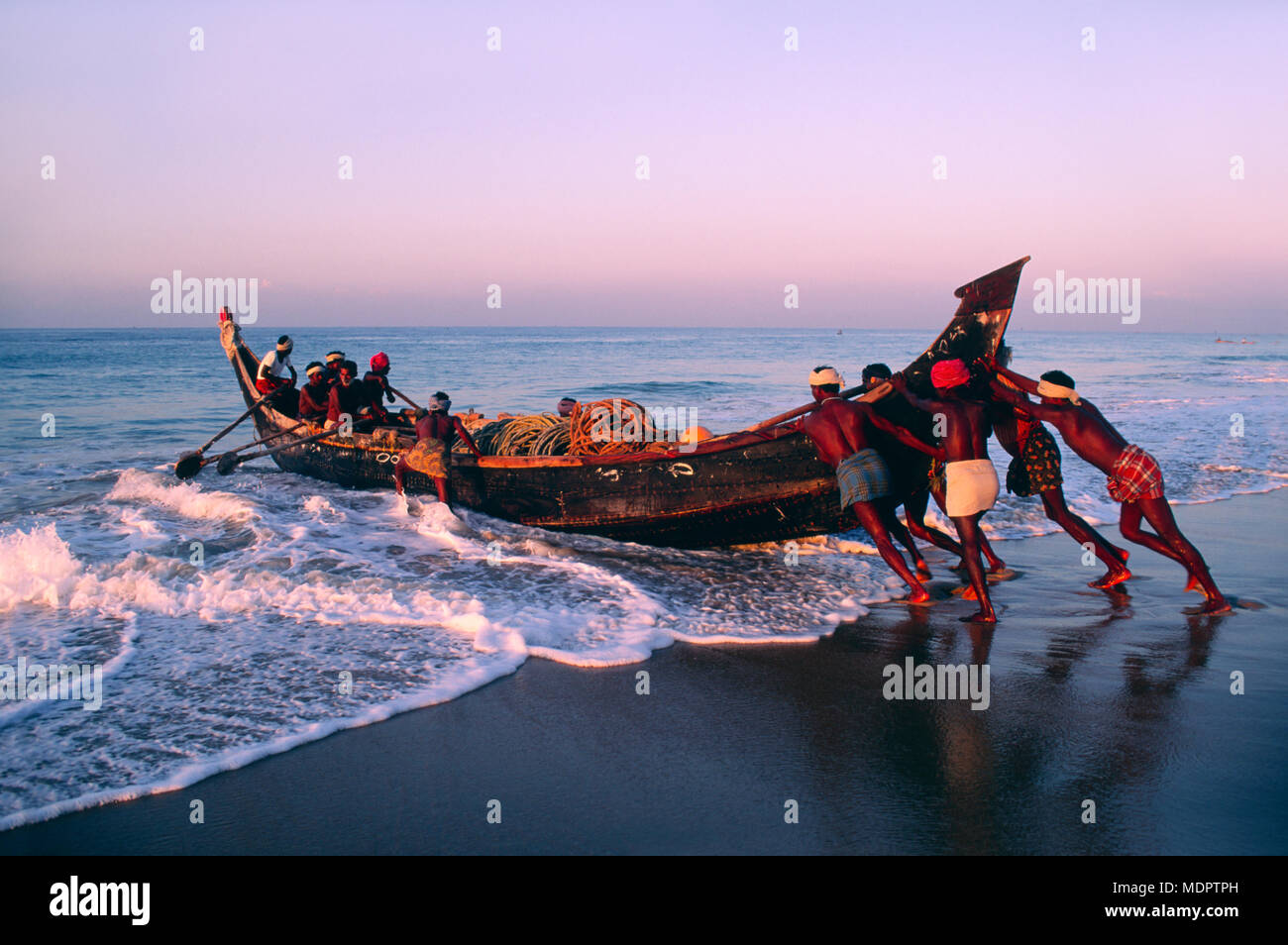 Kerala, India; fishermen pushing their boat into the sea at dawn Stock ...