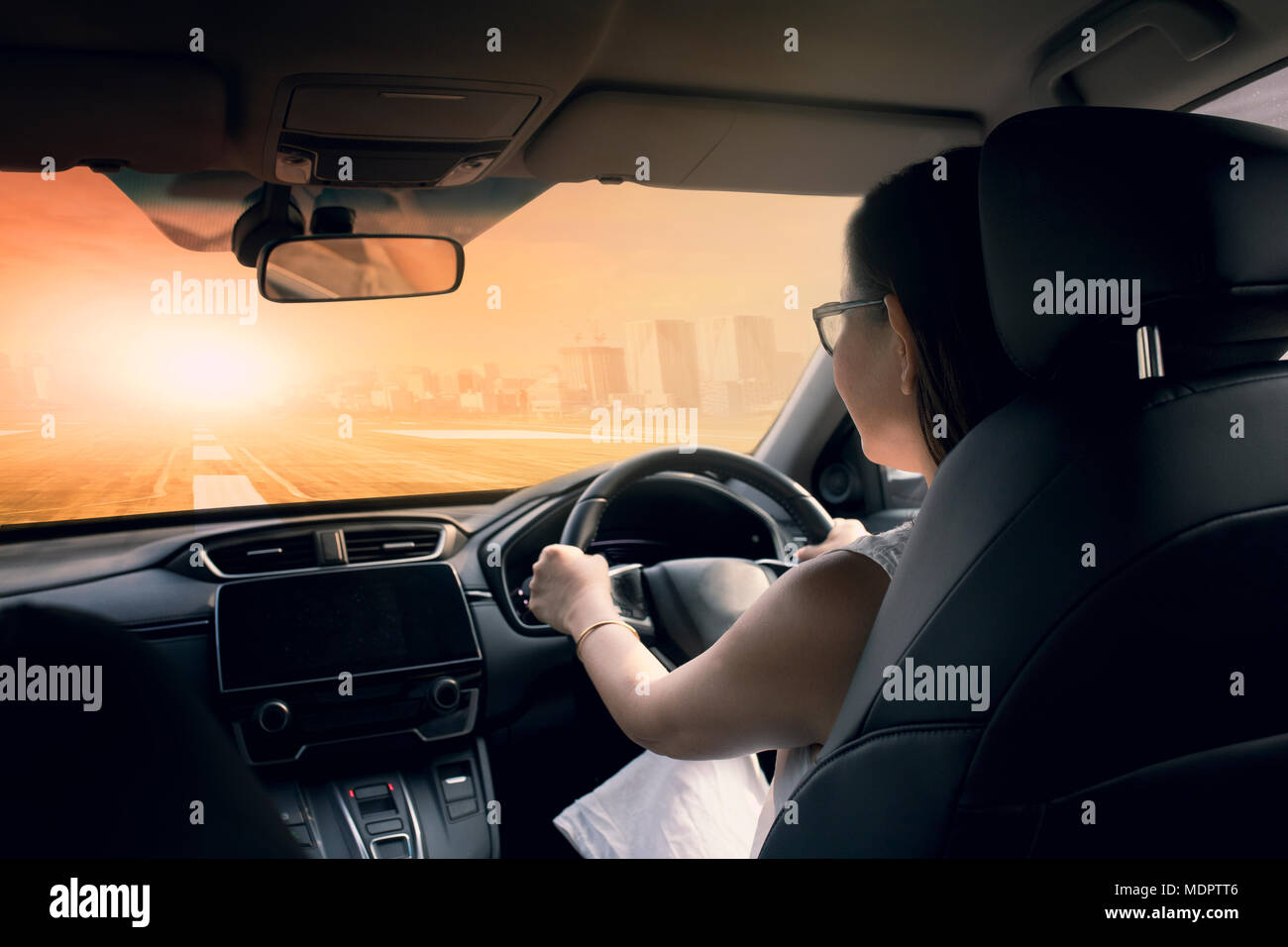 woman driving car on urban highway against sun light and city building ...